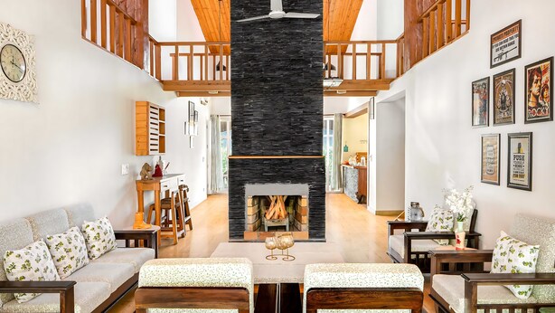 Uma sala de estar ampla com lareira, vigas de madeira no teto e uma escada para o andar superior.