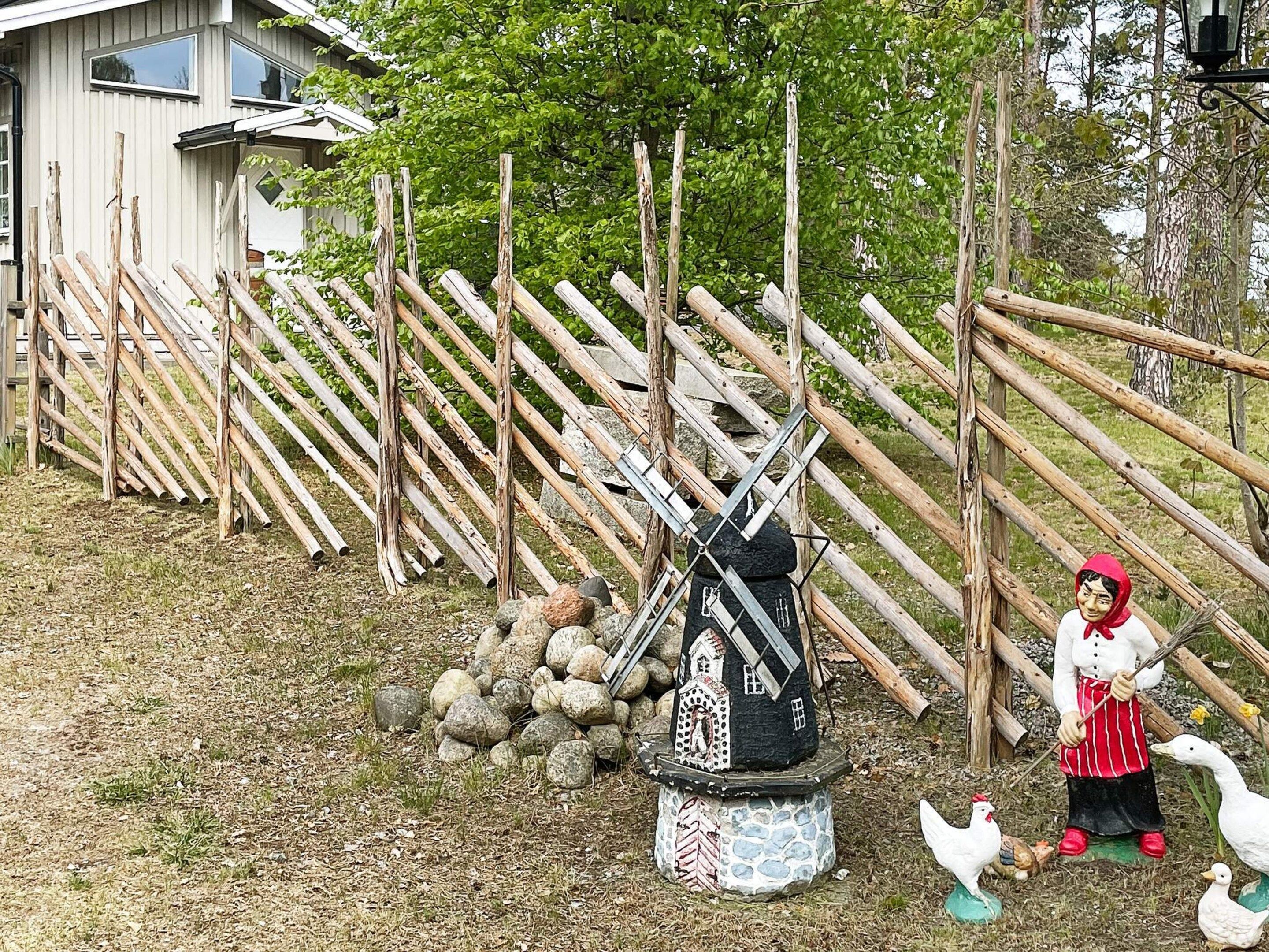 Cena campestre com um moinho, uma estátua de uma figura com chapéu vermelho e uma cerca de madeira.