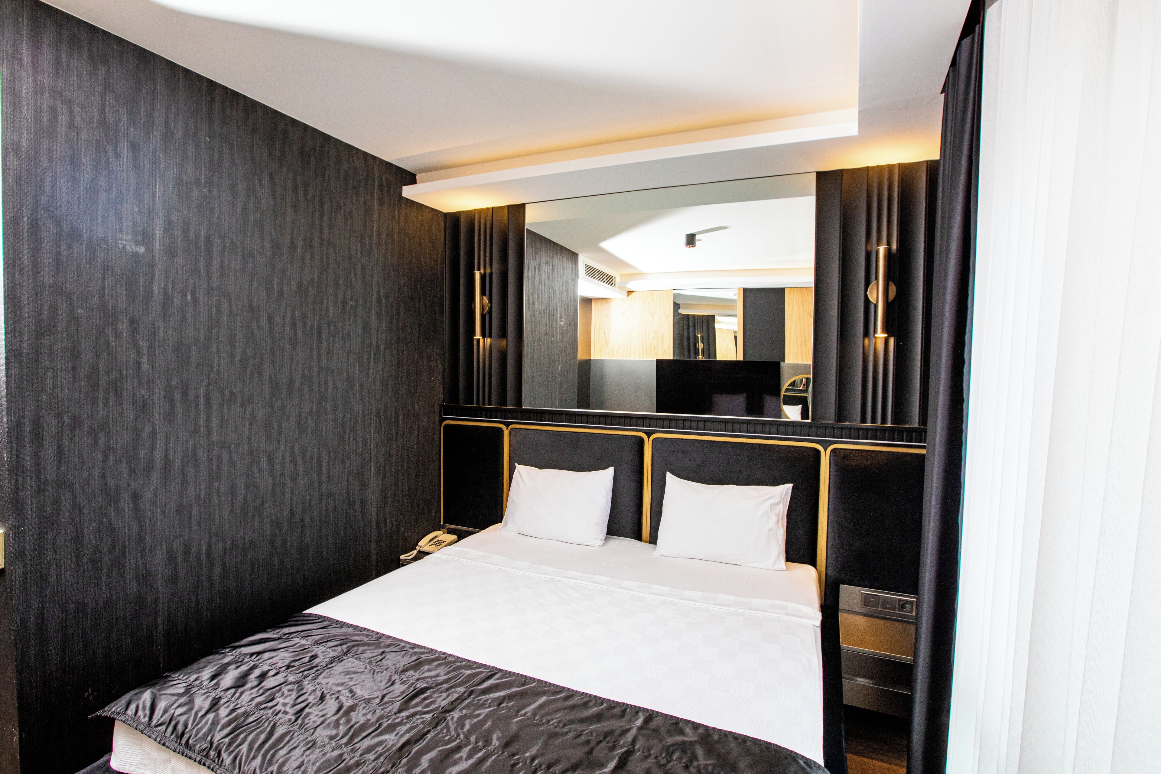 Quarto de hotel moderno com uma cama grande, telefone ao lado da cama e espelho sobre a cama.