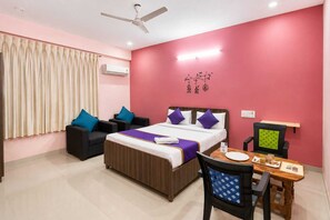 Quarto de hotel com cama, duas cadeiras, mesa, ventilador de teto e janela com cortinas.