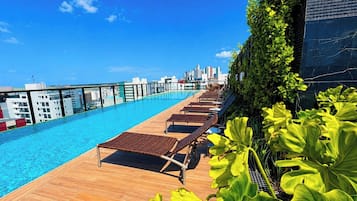 Piscina no terraço com espreguiçadeiras e vista para a cidade.