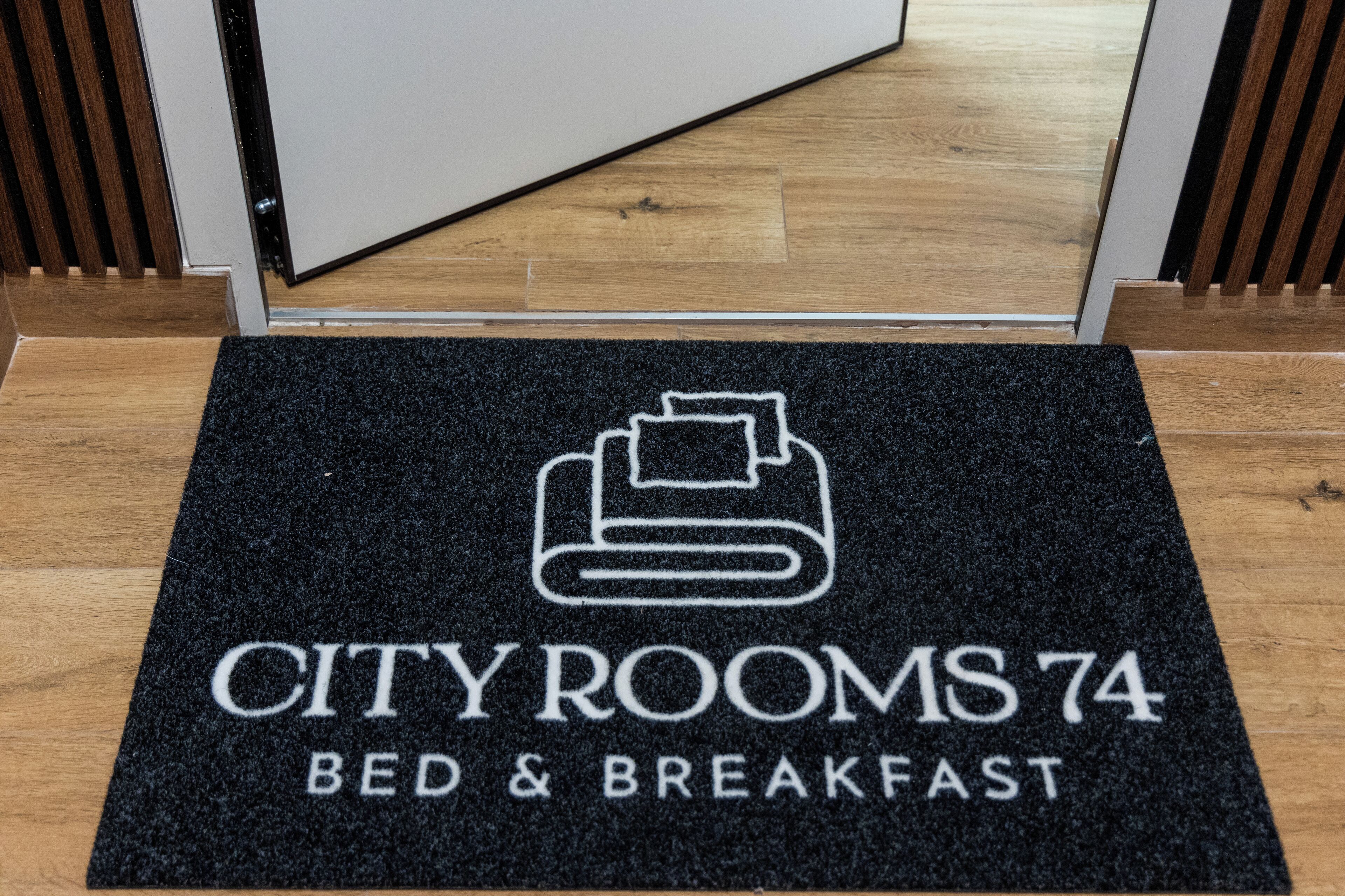 Tapete preto com o texto "CITY ROOMS 74 BED & BREAKFAST" e um ícone de cama.