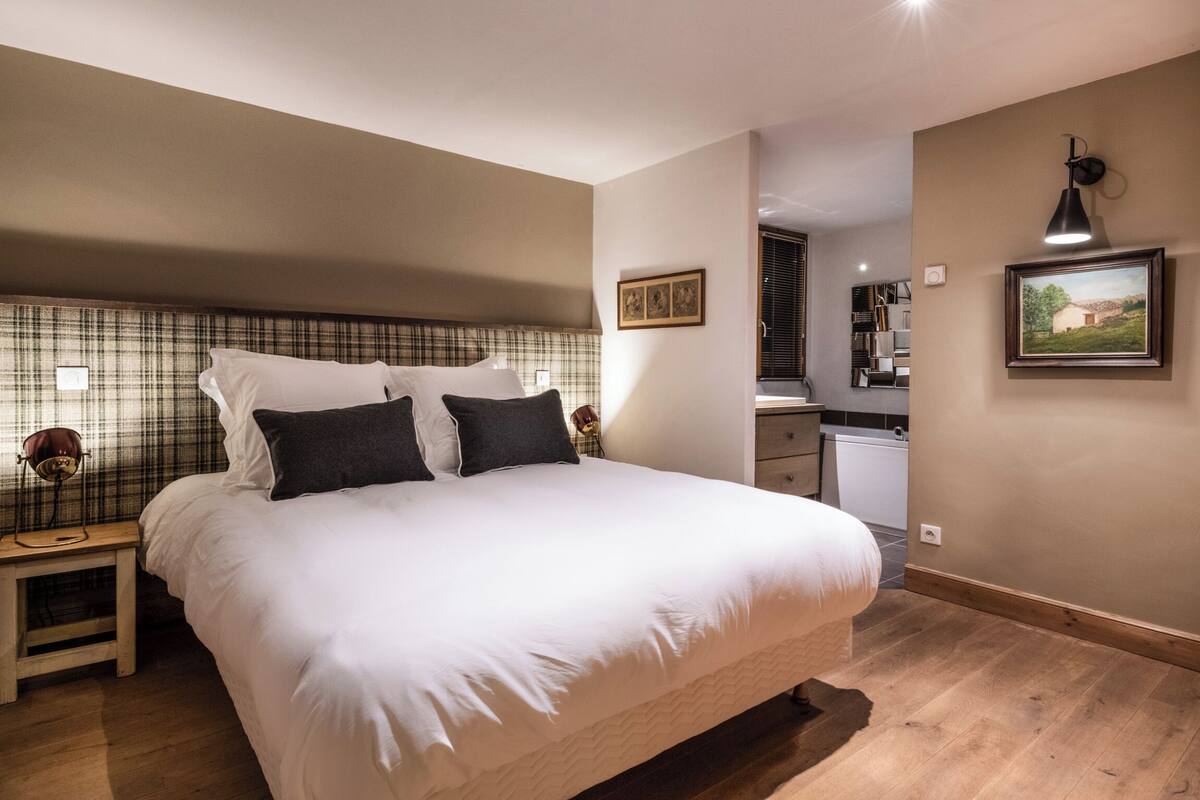 Quarto com cama grande, mesas de cabeceira, mesa de apoio e uma cadeira.