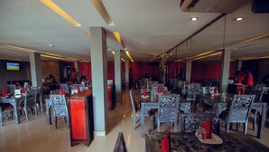 Restaurante com várias mesas e cadeiras, área de bar e uma tela de televisão ao fundo.