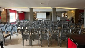 Sala de conferência com fileiras de cadeiras, um quadro branco e uma área de recepção ao fundo.