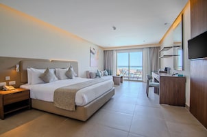 Quarto de hotel moderno com uma cama grande, uma escrivaninha, uma cadeira, uma televisão e varanda com vista.