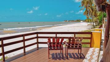 Um deck de madeira com duas cadeiras Adirondack com vista para a praia.