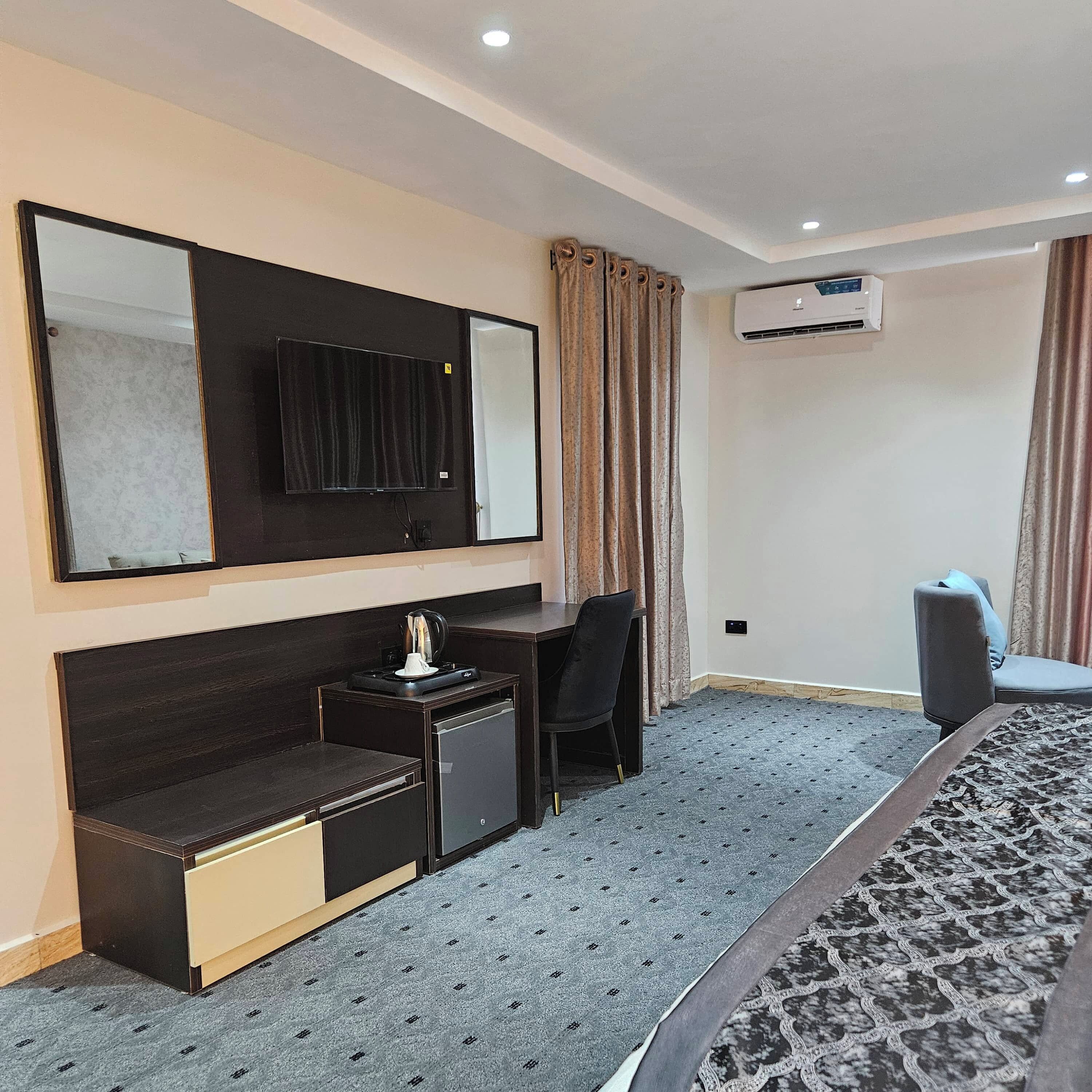 Quarto de hotel com uma cama grande, uma escrivaninha com cadeira, televisão e ar condicionado.