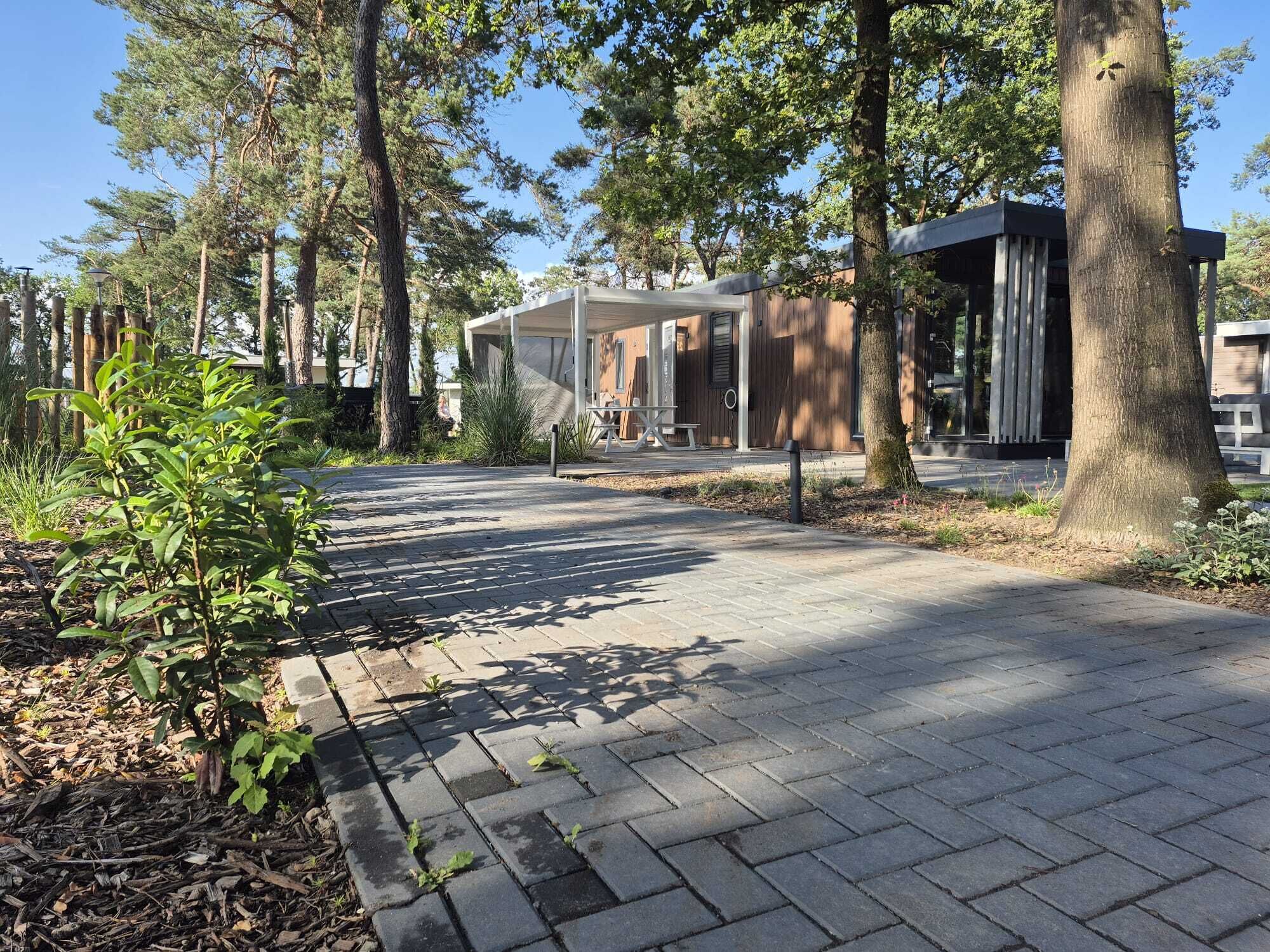 Uma trilha pavimentada conduz a um edifício moderno com fachada de madeira e área de estar coberta ao ar livre.