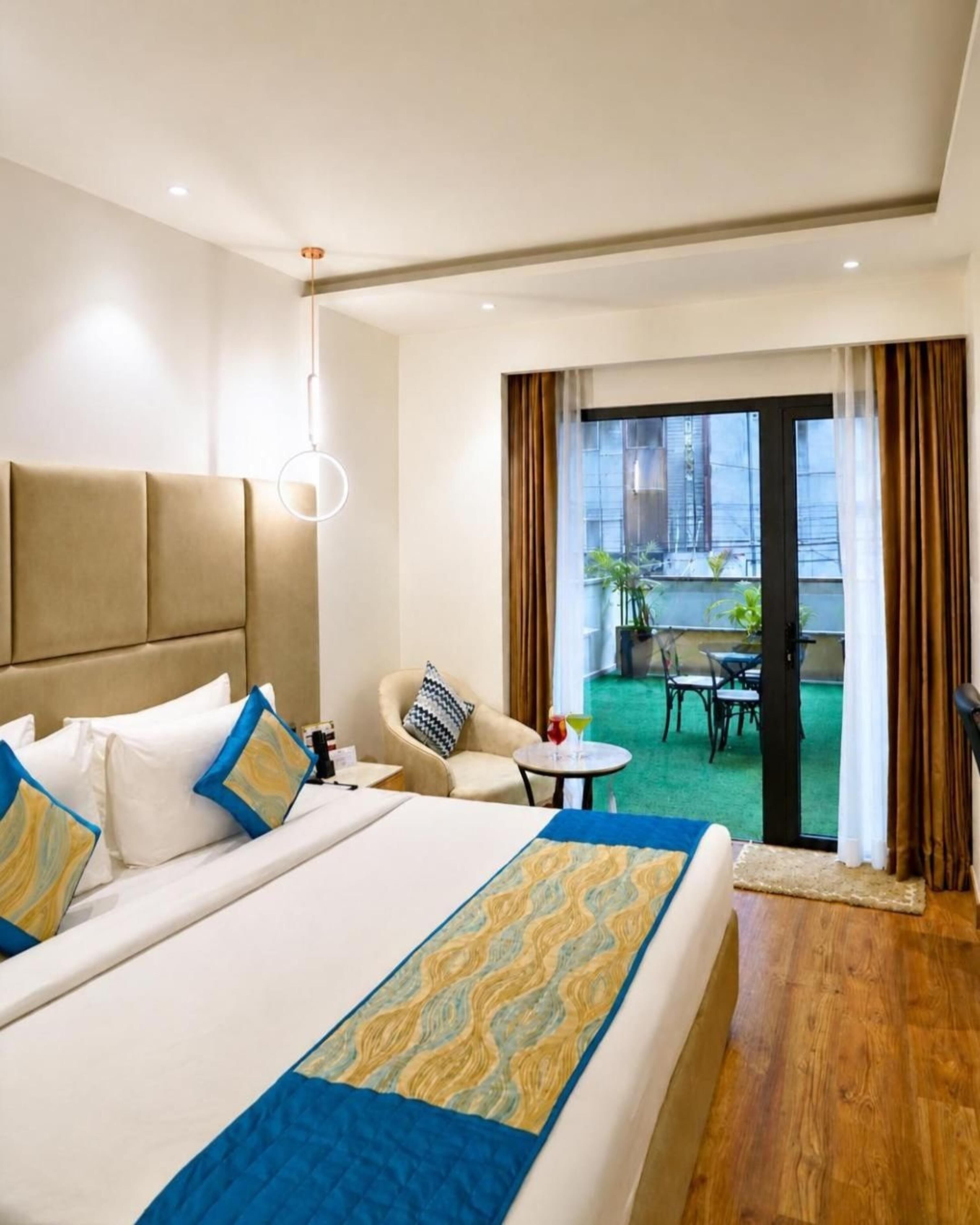 Quarto de hotel com uma cama grande, um espaço de estar com mesa e cadeiras, e vista para o exterior.