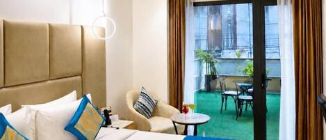 Quarto de hotel com uma cama grande, um espaço de estar com mesa e cadeiras, e vista para o exterior.