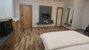 Quarto de hotel moderno com piso de madeira, cama, televisão presa à parede, escrivaninha com computador e espelho.
