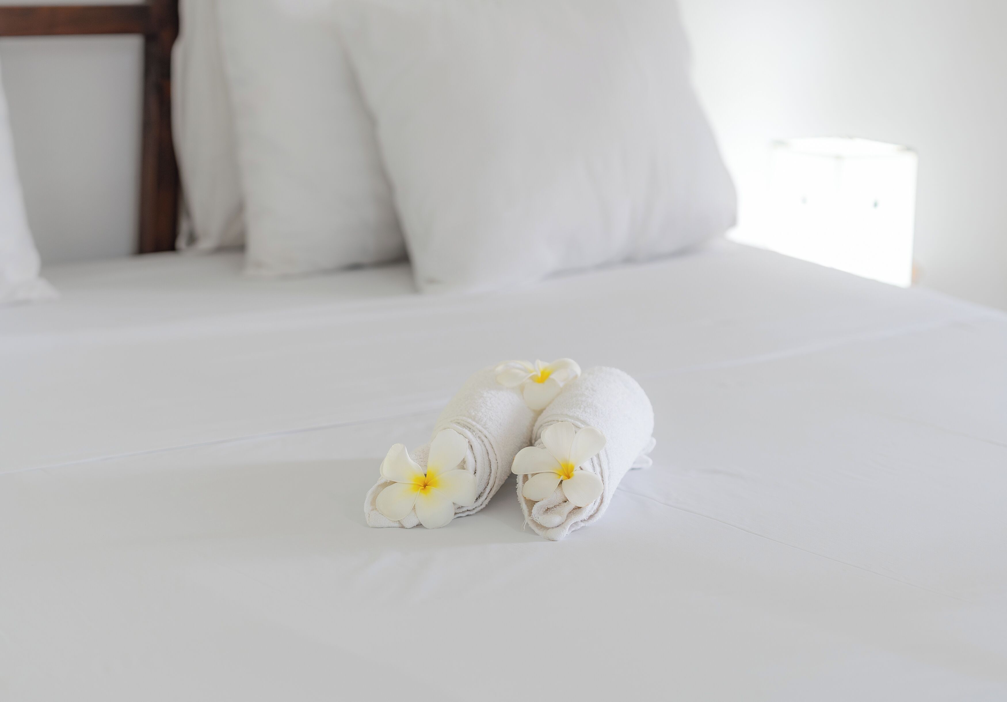 Cama bem arrumada com lençóis brancos e um par de toalhas com flores amarelas.