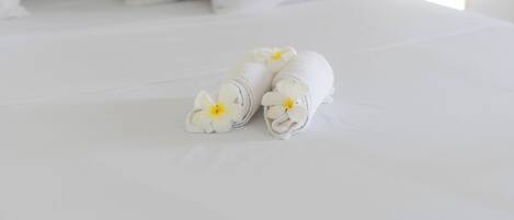 Cama bem arrumada com lençóis brancos e um par de toalhas com flores amarelas.