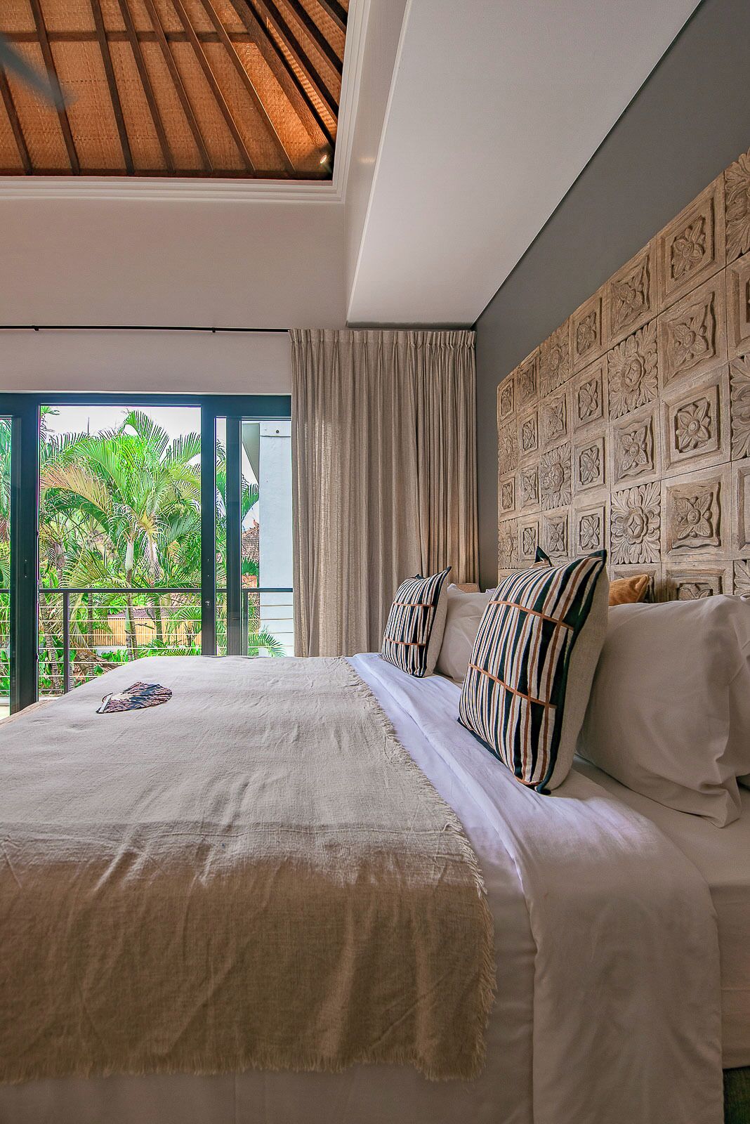Quarto com uma cama grande, vista para o verde lá fora e um painel decorativo na parede.