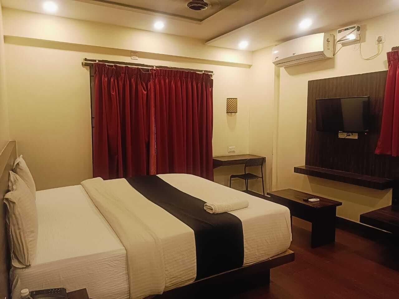 Quarto de hotel com uma cama, uma mesa, uma cadeira, uma televisão e um ar condicionado.
