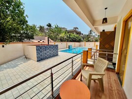 Uma área de piscina no terraço, com piso ladrilhado, piscina azul e deck de madeira.