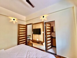 Quarto com cama, TV fixada em um painel de madeira e banheiro visível através de uma porta aberta.