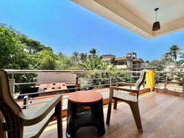 Uma varanda com mesa e cadeiras, guarda-corpo e vista para edifícios e árvores.