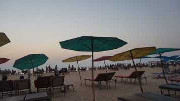 Uma praia com fileiras de cadeiras e guarda-sóis de praia, areia dourada e pessoas ao longe.