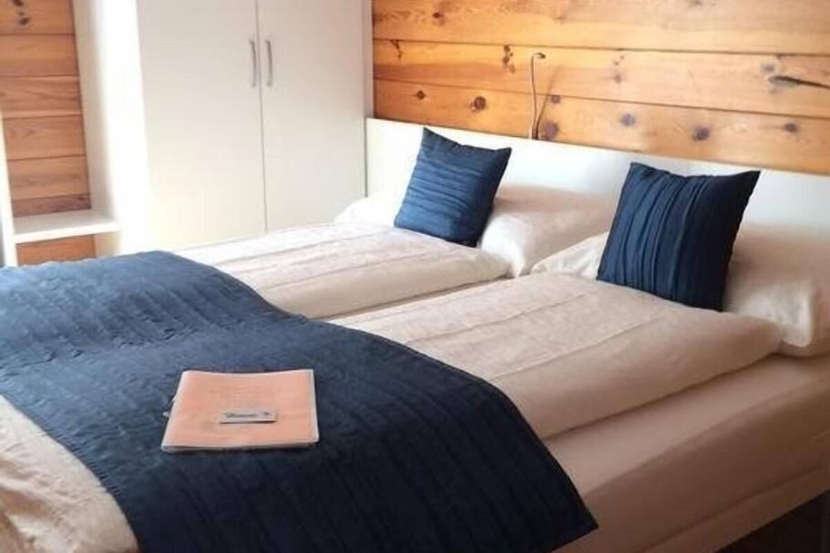 Uma cama de casal com um edredom azul e branco, um cobertor azul escuro e um livro pequeno sobre a cama.