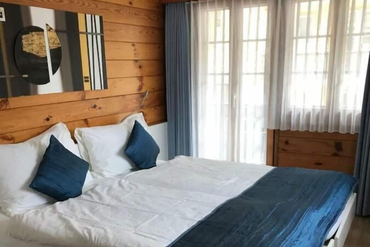 Cama com cabeceira de madeira, roupa de cama branca e detalhes em azul.
