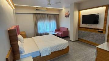 Quarto de hotel moderno com cama, mesa de cabeceira, TV e área de estar.