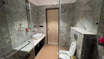 Um banheiro moderno com chuveiro em box de vidro, vaso sanitário branco e pia.