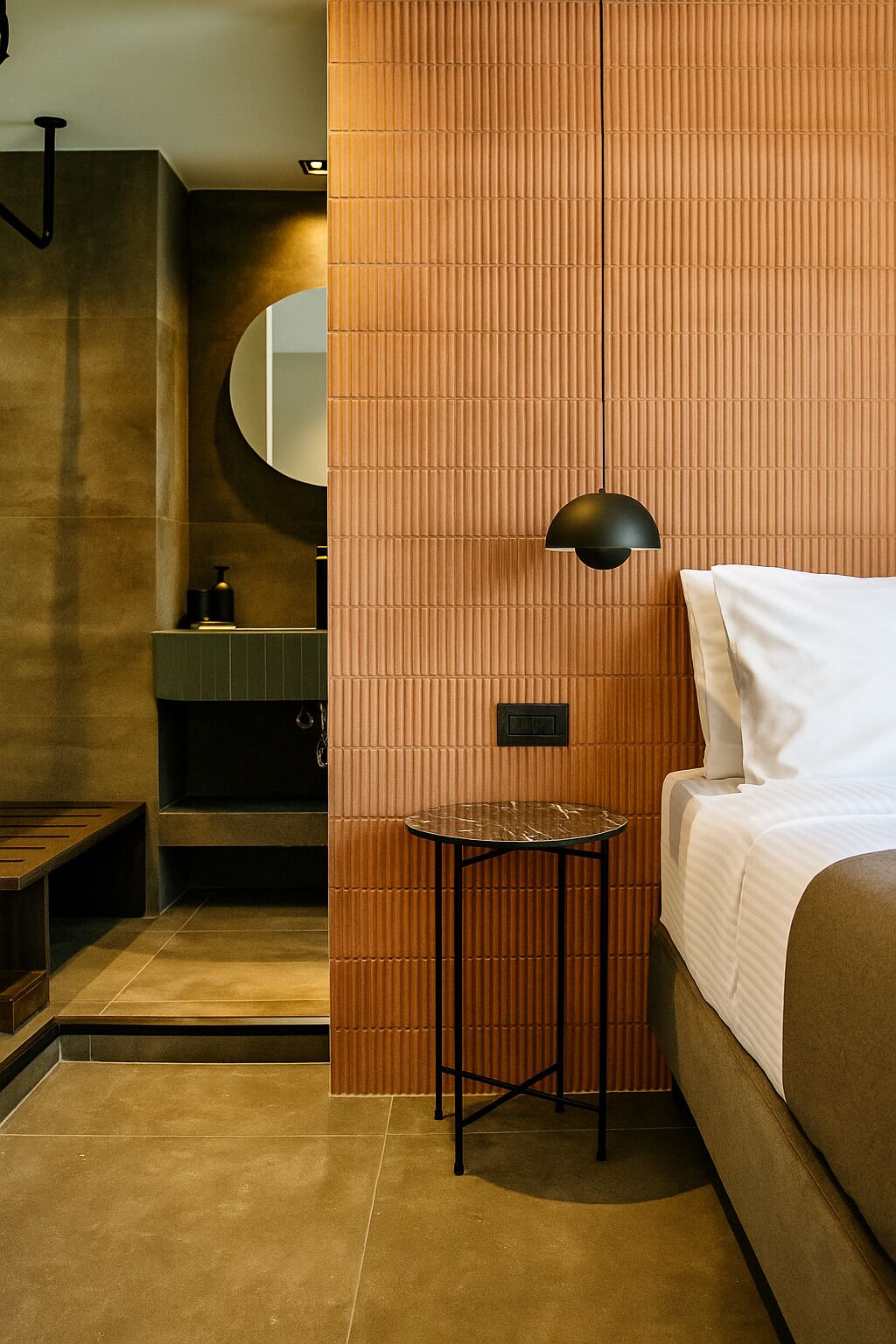 Quarto moderno com cama, mesa de cabeceira, espelho redondo e luminária na parede.