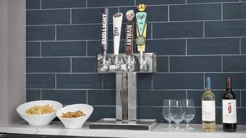 Uma área de bar com torneiras de cerveja, copos, tigelas de petiscos e garrafas de vinho.