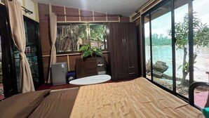 Quarto com uma cama grande, uma escrivaninha pequena, uma cadeira, uma janela com vista para a praia e um ventilador de teto.