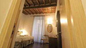 Um quarto com cama, cadeira, escrivaninha, espelho e janela com cortinas.