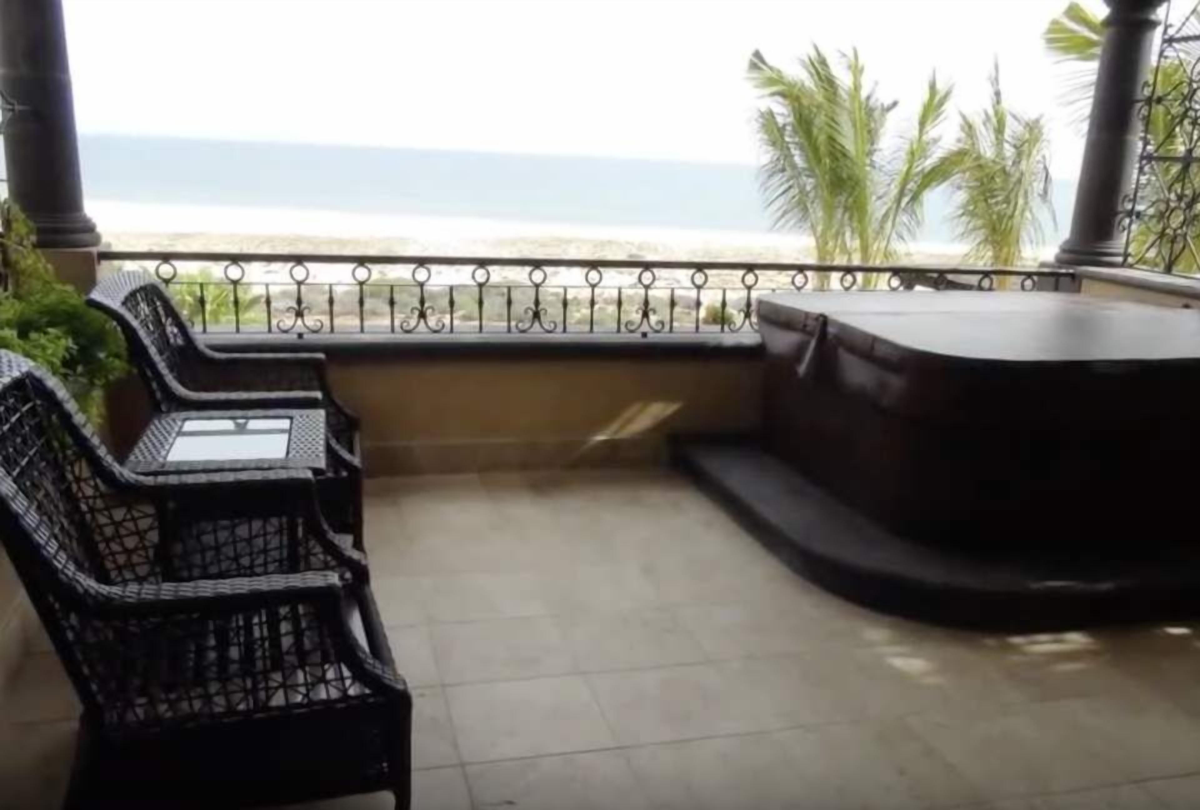 Uma varanda com vista para o oceano, uma cadeira de metal preta e uma mesa pequena.