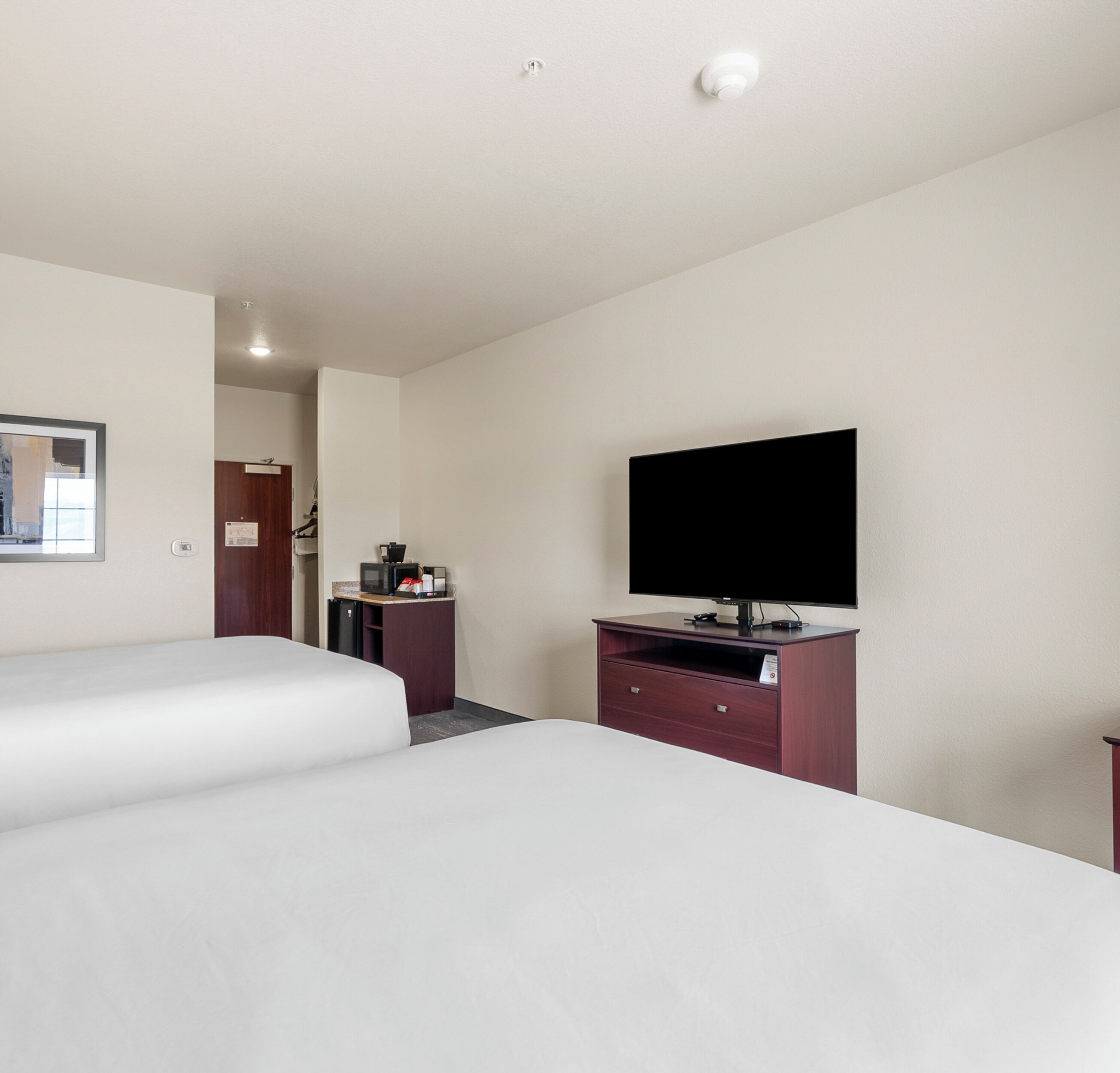 Quarto de hotel com duas camas, televisão, escrivaninha com micro-ondas e um pequeno frigorífico.