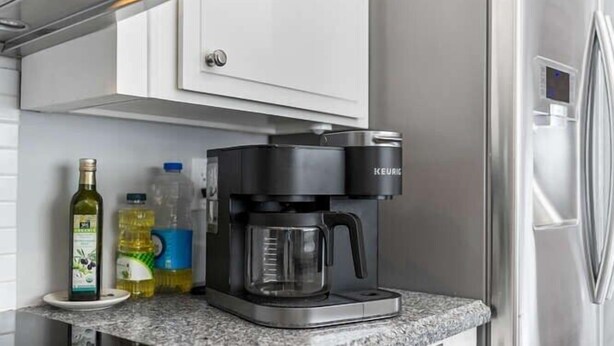 Cozinha moderna com uma cafeteira Keurig, uma garrafa de azeite e um recipiente de óleo de cozinha na bancada.
