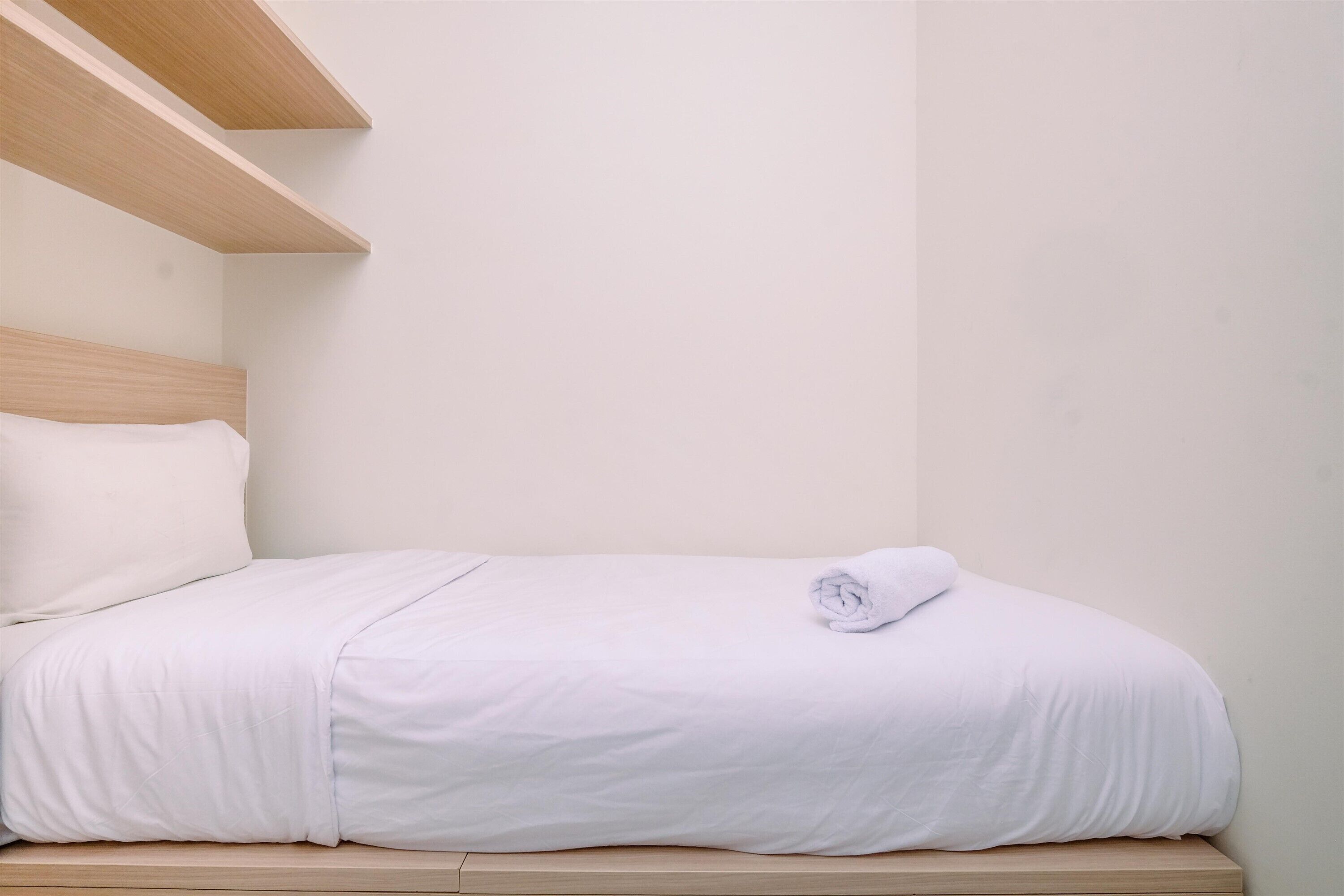 Cama bem arrumada com roupa de cama branca e cabeceira de madeira em um quarto minimalista.