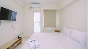 Quarto de hotel com cama, televisão fixada na parede, mesa de cabeceira de madeira e janela com cortinas.