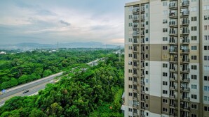 Um edifício alto com várias varandas, uma estrada com veículos e uma paisagem verde ao fundo.