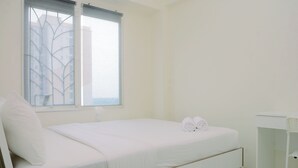 Quarto individual com janela, mesa de cabeceira e uma cadeira.