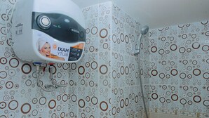 Casa de banho com azulejos estampados, secador de cabelo fixado na parede e mangueira de chuveiro.