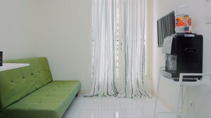 Quarto com sofá verde, um dispensador de água e uma TV sobre um suporte.