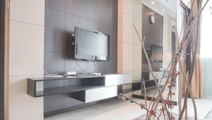 Uma sala de estar moderna com uma televisão de tela plana presa a uma parede escura, um console de mesa minimalista e um espelho grande refletindo o espaço.
