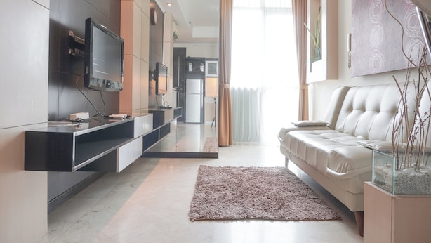 Uma sala de estar moderna com sofá, televisão na parede, área de cozinha e uma janela grande com cortinas.