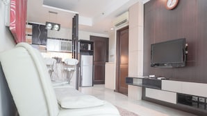 Uma sala de estar moderna com um sofá, uma televisão de tela plana na parede e uma área de cozinha ao fundo.
