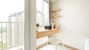 Uma varanda com vista para edifícios altos, uma escrivaninha com cadeira e uma pequena planta.