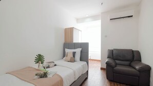 Quarto com cama, sofá cinza, guarda-roupa e planta em vaso.