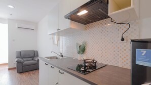 Uma cozinha moderna com armários brancos, sofá cinza, painel de parede estampado e fogão embutido.