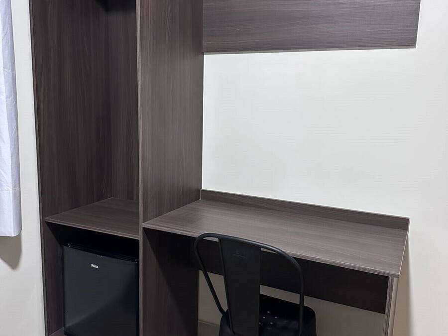 Quarto de canto com escrivaninha embutida, uma cadeira e um pequeno frigorífico.