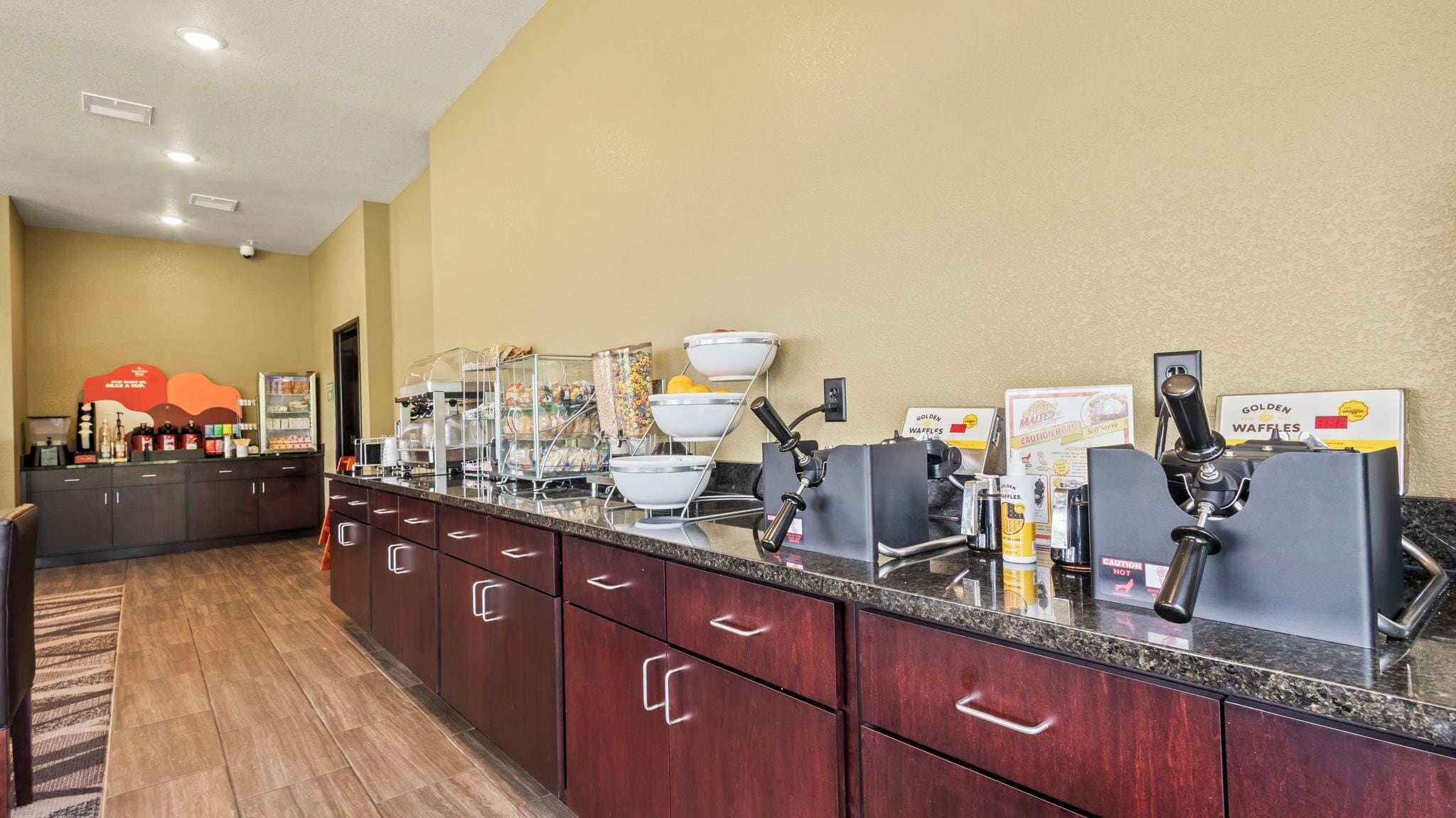 Espaço de pequeno-almoço de serviço próprio com diversas opções de comida, incluindo waffles e cereais.