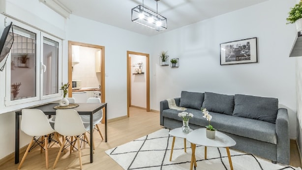 Uma sala de estar moderna com um sofá cinzento, uma mesa de jantar com cadeiras, uma mesa de centro e uma luminária pendente.